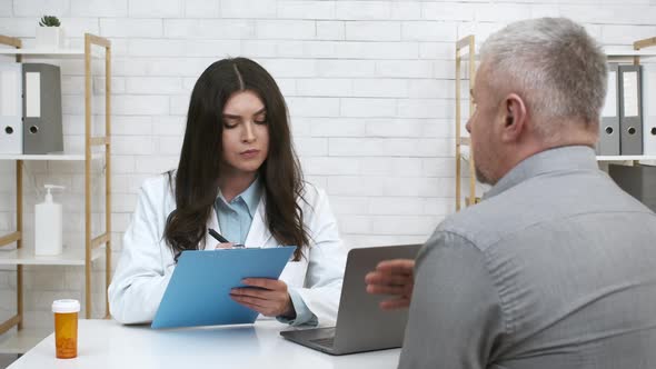 Practitioner Talking With Sick Senior Patient Taking Notes In Office ...