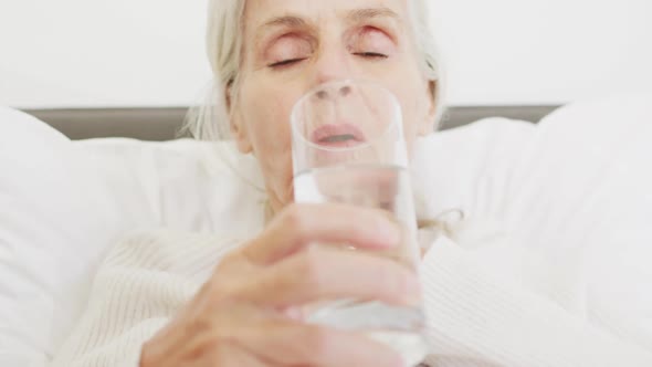 Video of caucasian senior woman drinking water in bed, Stock Footage