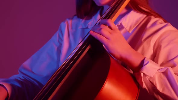 Talented woman playing the cello on neon background, side view, closeup ...