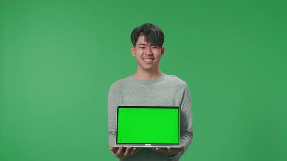 A Smiling Asian Man Holding Green Screen Computer While Standing In ...