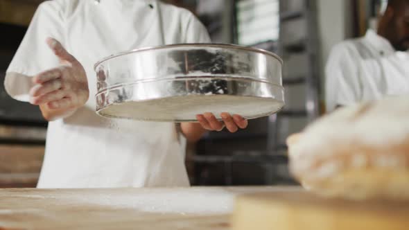 Animation of midsection of asian female baker sieving flour on board ...