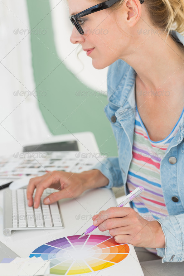 Happy designer working at her desk using a colour wheel in creative ...
