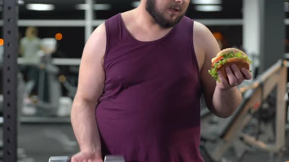 Fat Man Lifting Dumbbell and Looking at Hamburger in Other Hand, Will ...