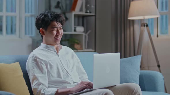 Smiling Asian Man Having Video Call On Laptop Computer While Sitting On ...