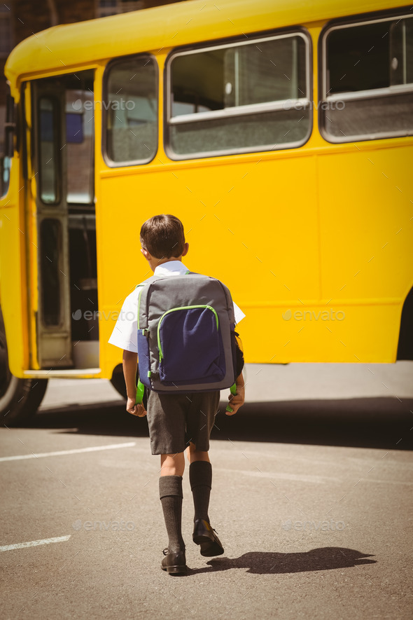 Cute pupil walking to the school bus outside the elementary school ...