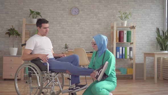 Muslim Doctor in Hijab Examines the Leg of a Disabled Person in a ...