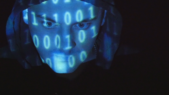 Hooded Hacker Working On A Computer Binary Code Projecting On His Face Source Code Projected