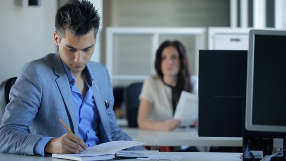 Male Realtor Consults With a Colleague In Office And Writes Information ...