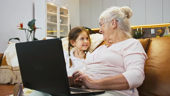 Granny Smiling and Talking to Granddaughter Typing on Laptop Sitting on ...