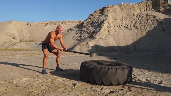 Bald Man Strongman Hits a Hammer on a Huge Wheel in the Sandy Mountains ...