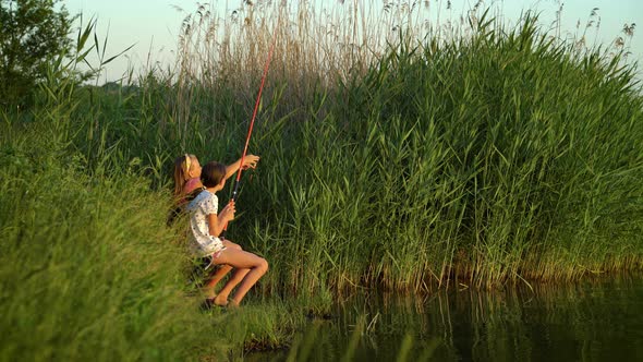 Little girls with fishing rods on river bank at sunset, Stock Footage
