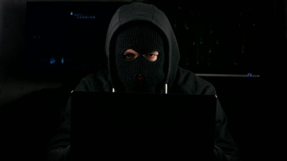 Dangerous Hacker In a Mask Working On a Computer In a Dark Office Room ...