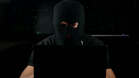 Dangerous Hacker In a Mask Working On a Computer In a Dark Office Room ...