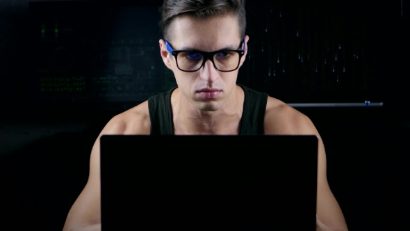Male Hacker With Glasses Working On a Computer In a Dark Office Room ...