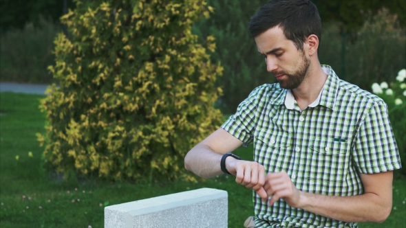 Young Man Using Smartwatch While Sitting On The Bench In The Park ...