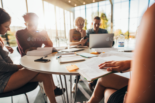 Young students sitting around a table in library Stock Photo by jacoblund