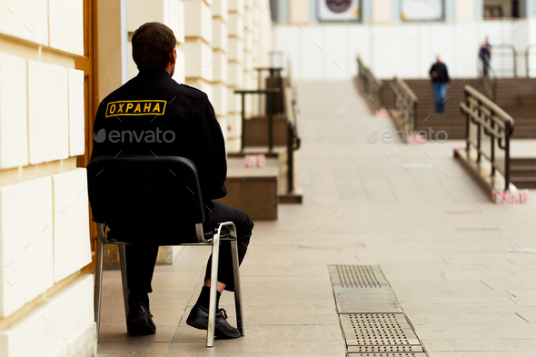 Security guard sitting on a chair at the entrance to the indoor Stock ...