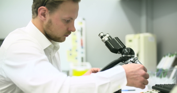 Scientist Is Looking Through Microscope and Writing Data on Tablet ...
