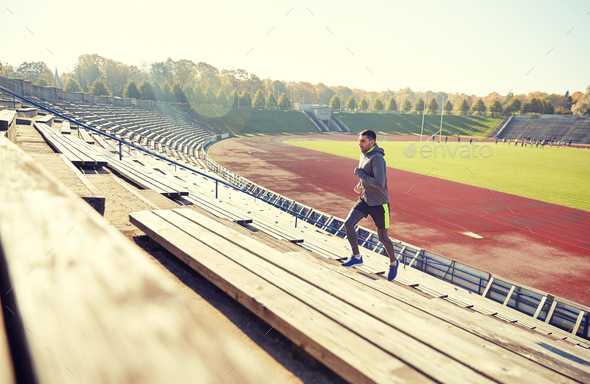 happy young man running upstairs on stadium Stock Photo by dolgachov