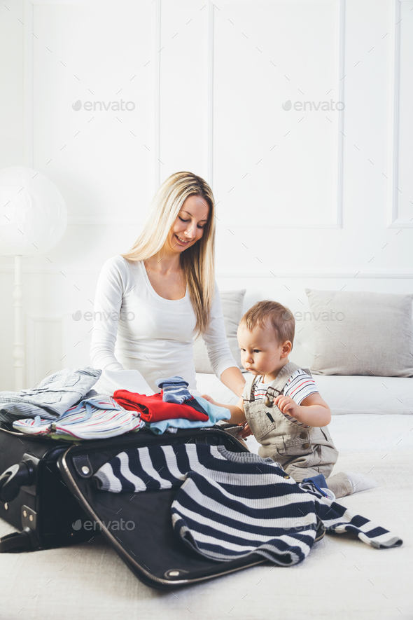 Travelling with kids. Happy mother with her child packing clothes for ...