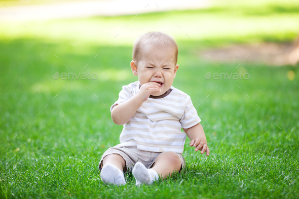 Little boy crying while sitting on grass in park Stock Photo by photobac