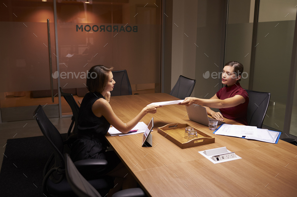 Two businesswomen working late in office passing documents Stock Photo ...