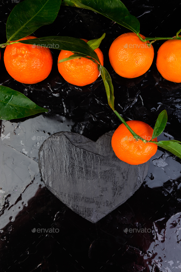 Tangerine around with black slate heart shaped. Stock Photo by bondarillia