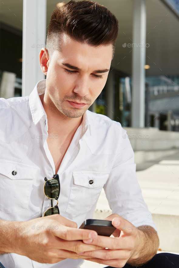 serious man looking at mobile phone sitting outside in city Stock Photo ...