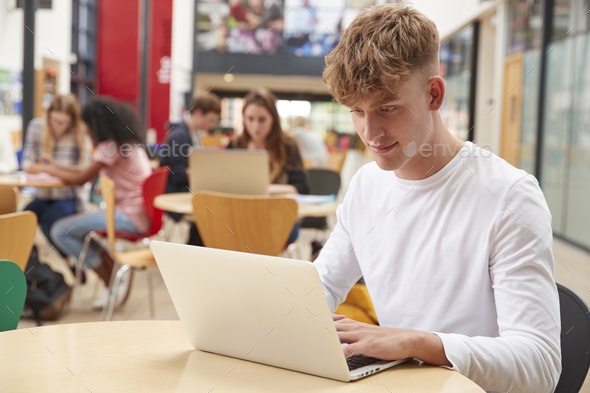 Male Student Working In Communal Area Of Busy College Campus Stock ...