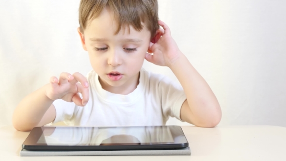Little Boy Sitting at Table, Playing with Tablet, The Child Is Playing ...