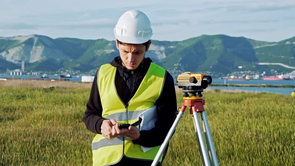 Surveyor Man in Green Work Clothes and Helmet Adjusts the Equipment ...