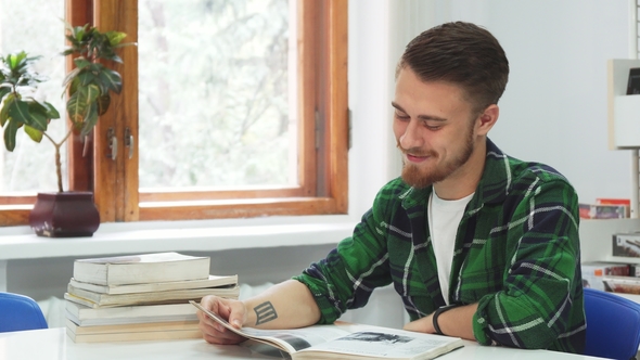 A Cute Guy Laughs at What He Read in the Book, Stock Footage | VideoHive