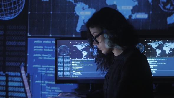 Portrait of Young Woman Programmer in Eyeglasses Working at a Computer in the Data Center Filled ...