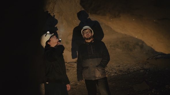Two Speleologists with Flashlight Exploring the Cave with Fear in ...