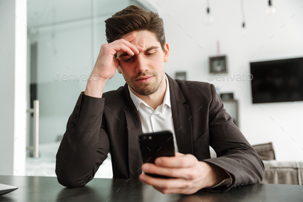 Serious young businessman using mobile phone. Stock Photo by vadymvdrobot