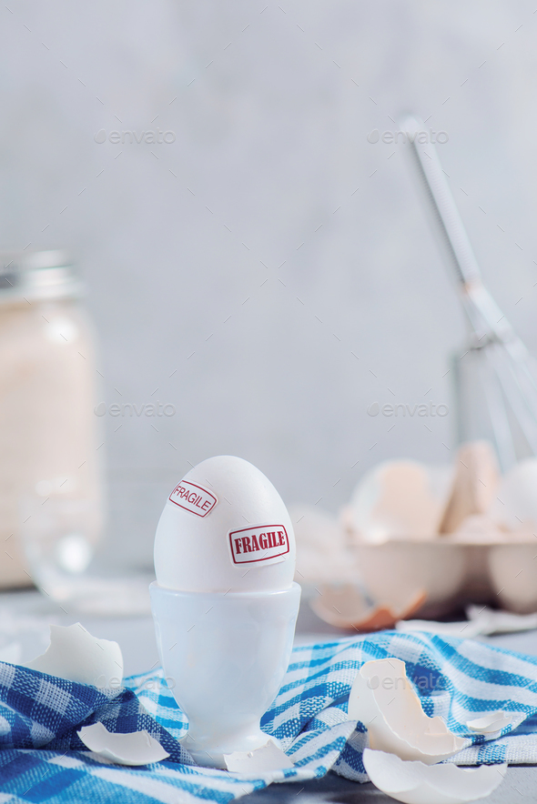 White egg in a porcelain egg stand with a red Fragile sign. High key ...