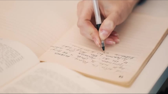 Girl Writes Down Something From a Book Sitting at the Table in a ...