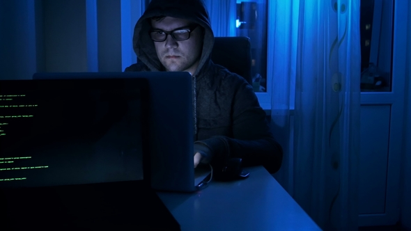 Footage of Young Male Hacker Wearing Eyeglasses and Hood Working at ...