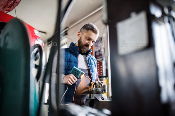 Man mechanic repairing a car in a garage. Stock Photo by halfpoint