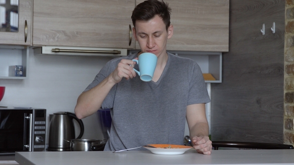 Young Man Eating Oatmeal Porridge and Coffee in the Kitchen, Stock Footage