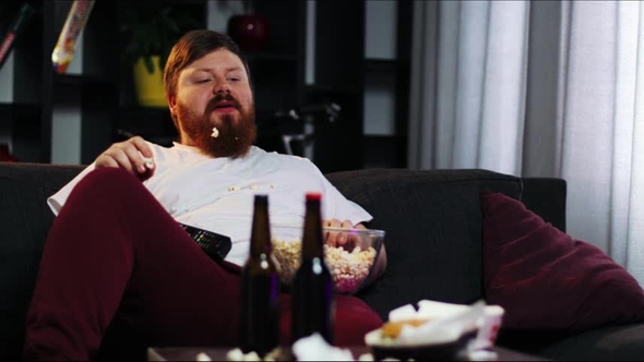 Smiling Fat Man with Beard Watches TV in the Room and Eats Pop-corn at ...