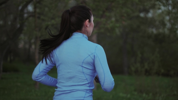 A Young Girl in Blue Sports Clothes Is Running Along the Evening Park ...