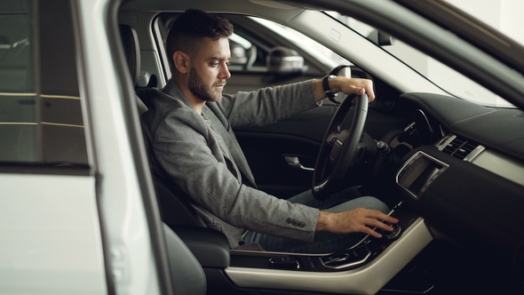 Serious Young Man Is Sitting Inside New Car in Motor Showroom and ...