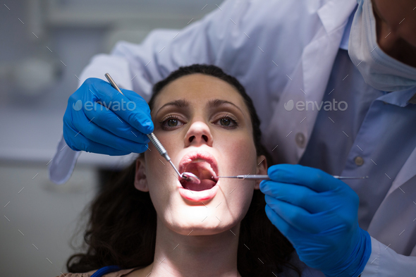 Dentist examining a female patient with tools Stock Photo by Wavebreakmedia