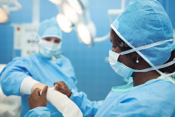 Female surgeon helping her co-worker in wearing surgical gloves Stock ...