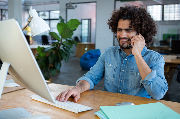Graphic designer using computer while talking on mobile phone Stock ...