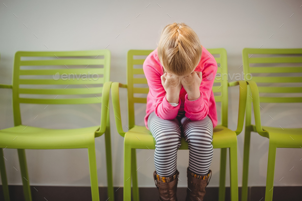 Upset girl sitting on chair in corridor Stock Photo by Wavebreakmedia