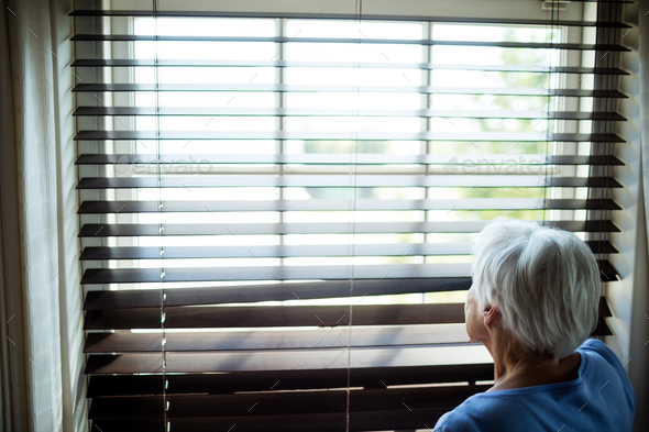 Senior woman looking out from window blind Stock Photo by ...