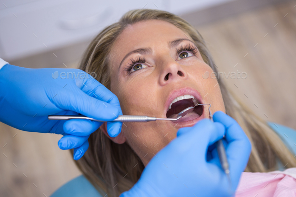 Dentist examining a female patient with tools Stock Photo by Wavebreakmedia