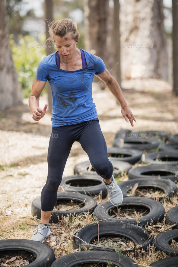 Woman running over the tyre during obstacle course Stock Photo by ...